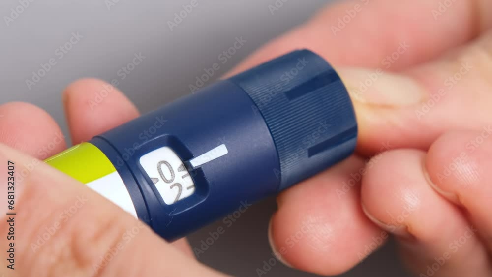 Close up on hands turn knob on insulin pen and dial up insulin dose for ...