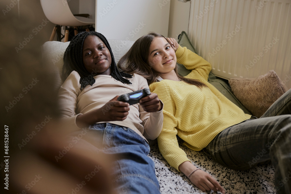 Smiling teenage girl holding game controller while lying down with ...