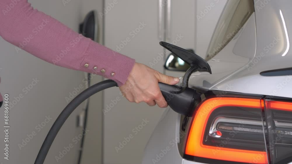 CLOSE UP: Woman plugs in a white BEV for charging motor battery in home ...