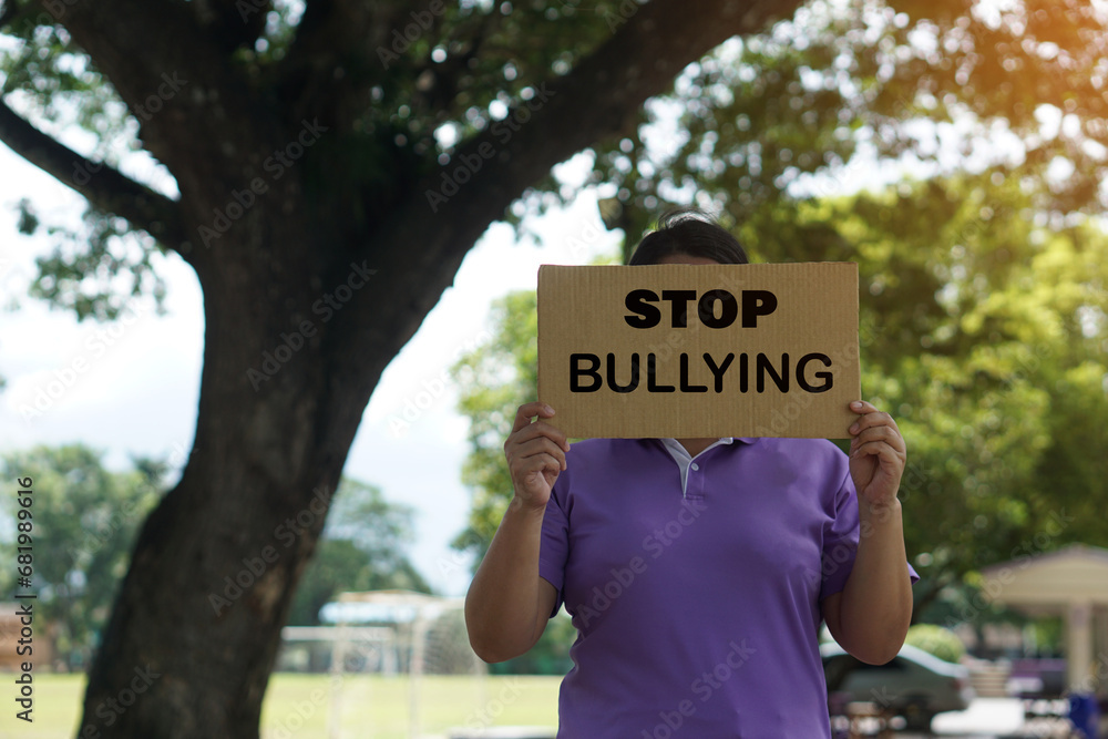 A woman holds paper placard with text Stop Bullying, outdoor background ...