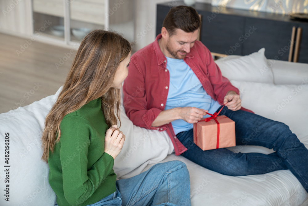 Romantic surprise. Contented man unpacking present gift box with woman ...