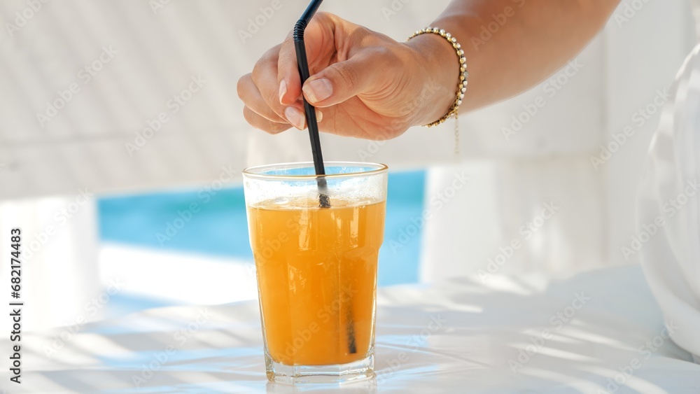 At a beach cafe, a woman stirs her orange juice with a straw, capturing ...