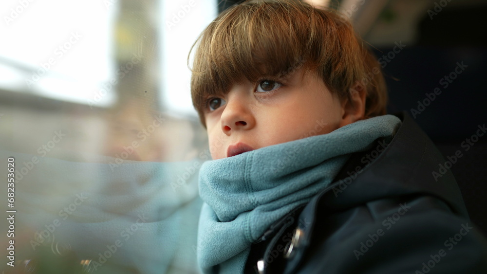 Playful child traveling by train leaning on window glass wearing scard ...