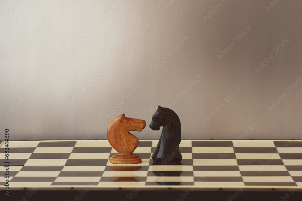 Two chess knights, one wooden and one marble, stand facing each other ...