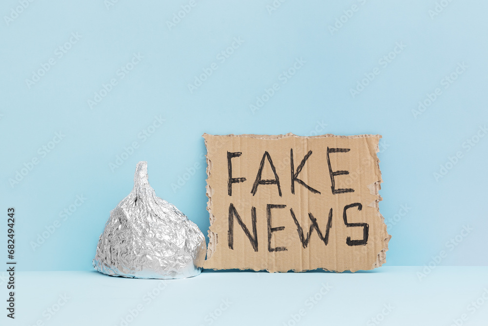 Aluminium foil hat and fake news poster on blue background, symbol for ...