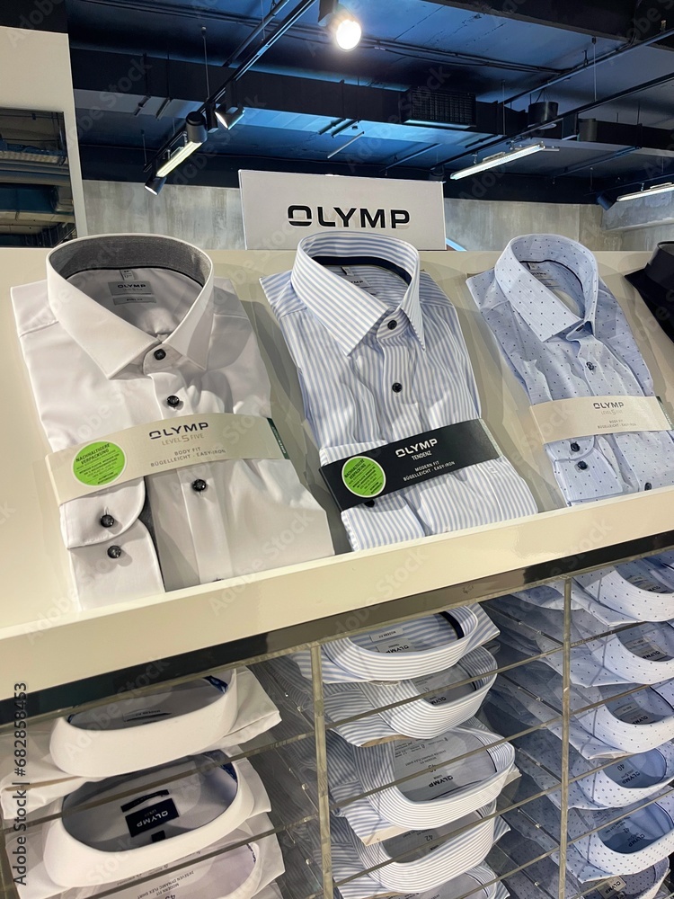 Men's shirts of famous brand OLYMP on counter in store. Contemporary shopping mall in urban loft ...