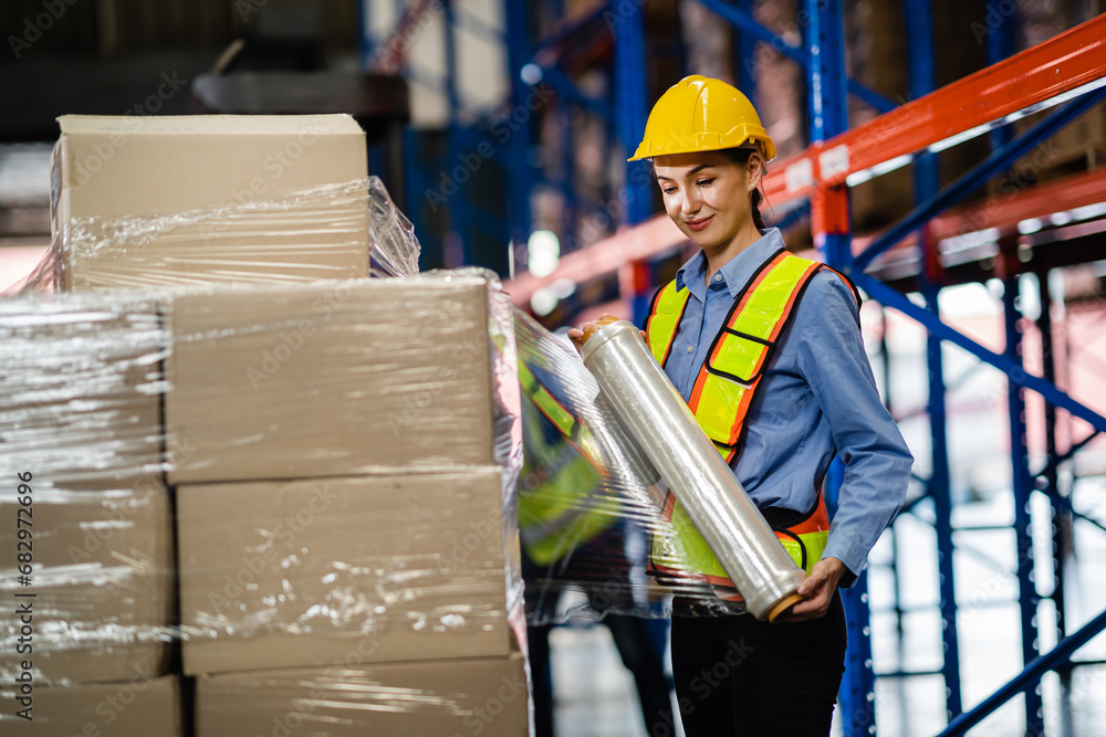 Warehouse workers wrap parcels in stretch film on pallets in a factory ...