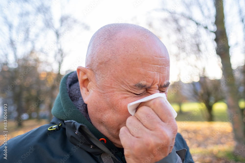 runny nose in adult, elderly man blowing nose into tissue while on walk ...