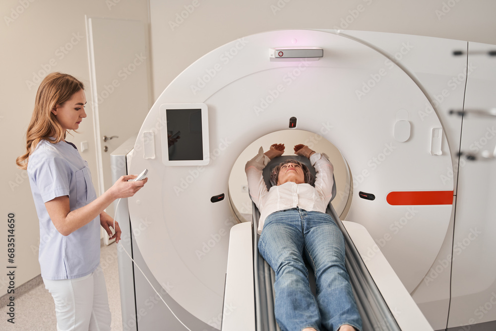 Senior lady laying on CT scan bed while female radiologic technician ...