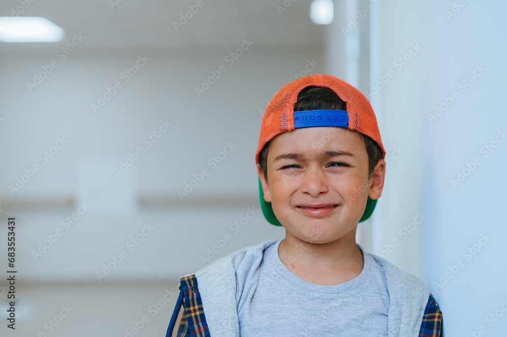 Crying little baby boy in baseball cap standing indoors looks at camera ...