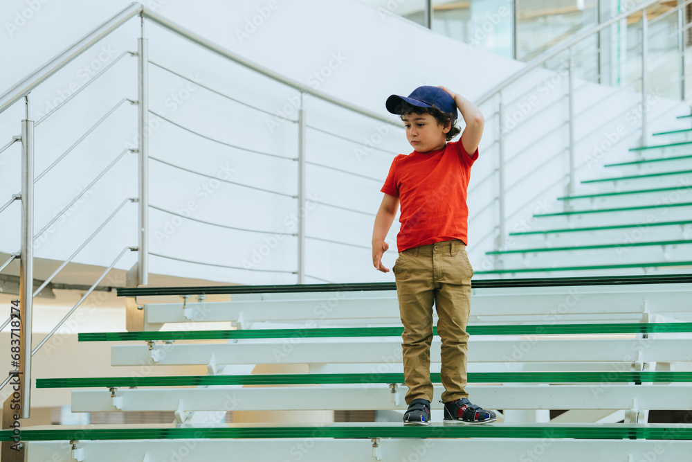 Pensive little boy in casual standing on stairs at shopping mall ...