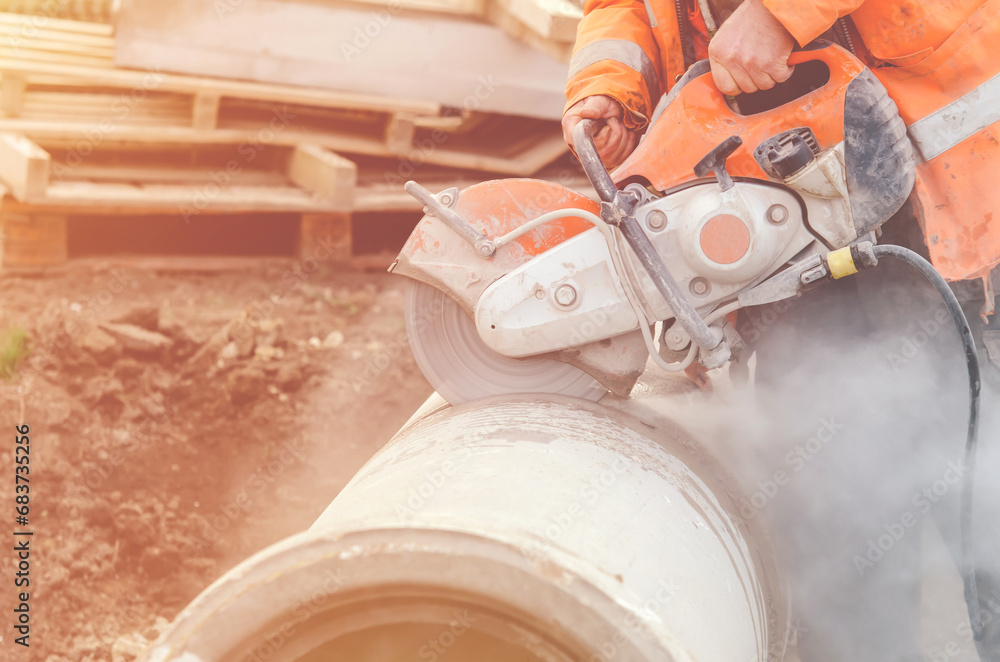 A worker at the construction site cutting a concrete drainage pipe with ...