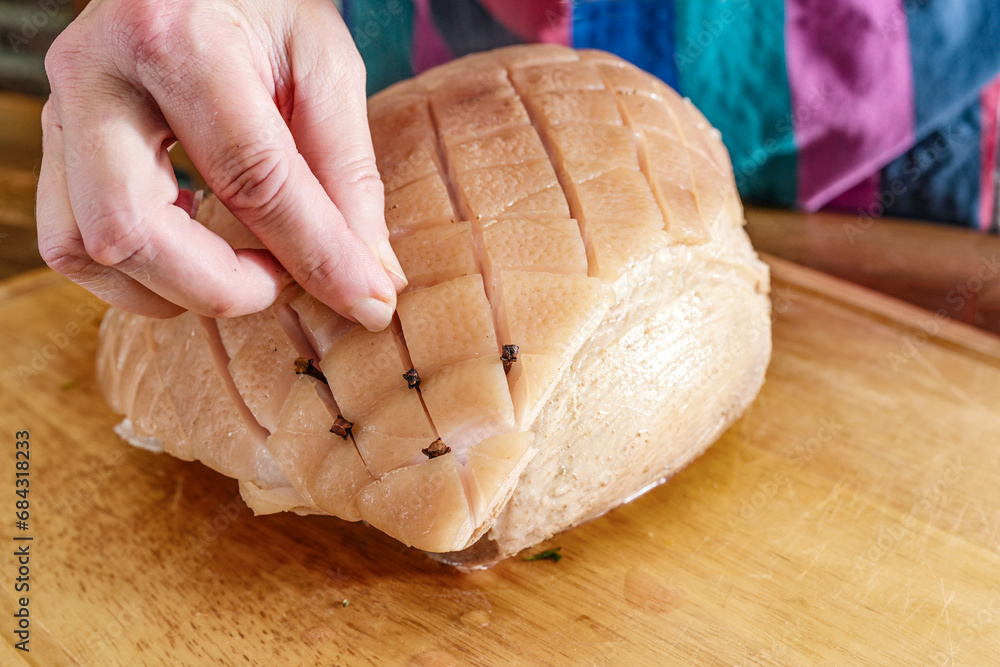 Hand of a woman larding the rind of a raw roast pork with cloves on a ...