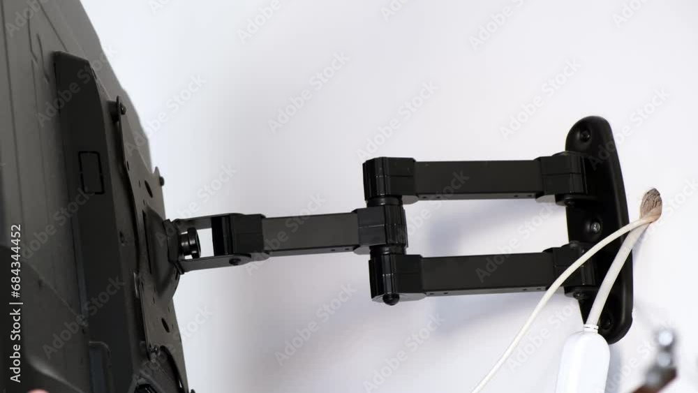 A man rotates a flat-screen TV hanging on a bracket, demonstrating a ...