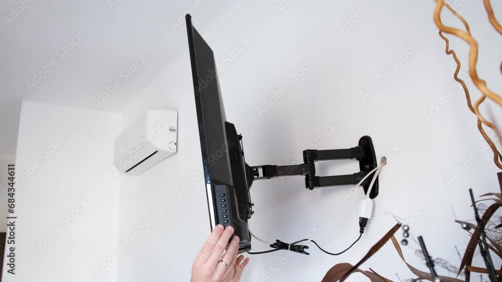 A man rotates a flat-screen TV hanging on a bracket, demonstrating a ...