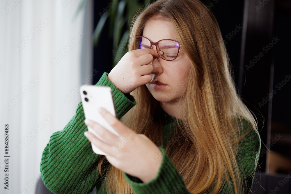 girl squinting with poor eyesight wearing glasses looking at a mobile ...