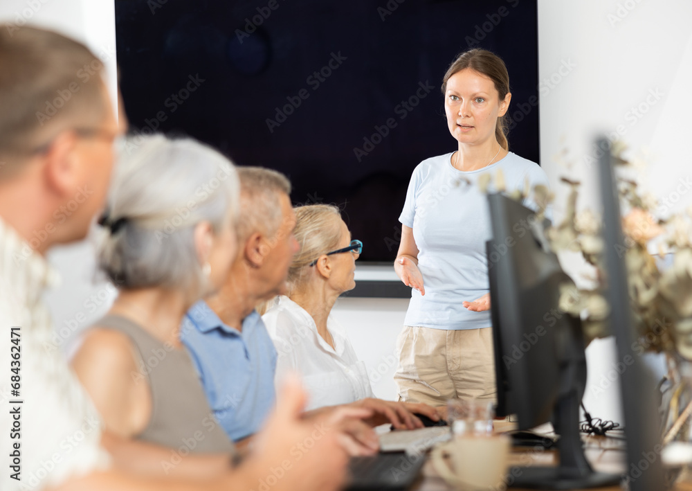 Adult female teacher showing group of elderly people how to work with ...