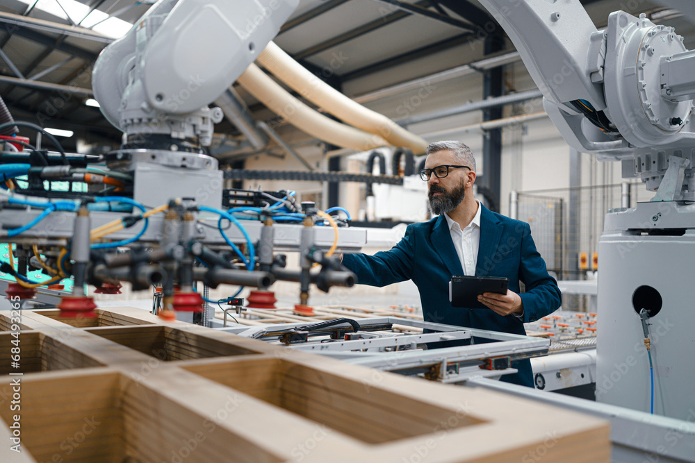 Male engineer in modern industrial factory, checking robotic arm ...