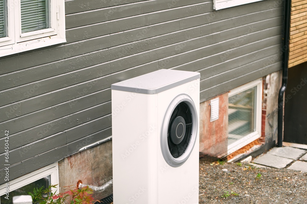 An air conditioner outdoor unit outside of a house in the grass. Modern ...