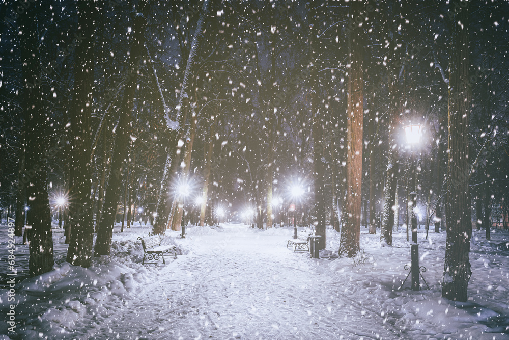 Foto de Snowfall in a winter park at night with glowing lanterns ...