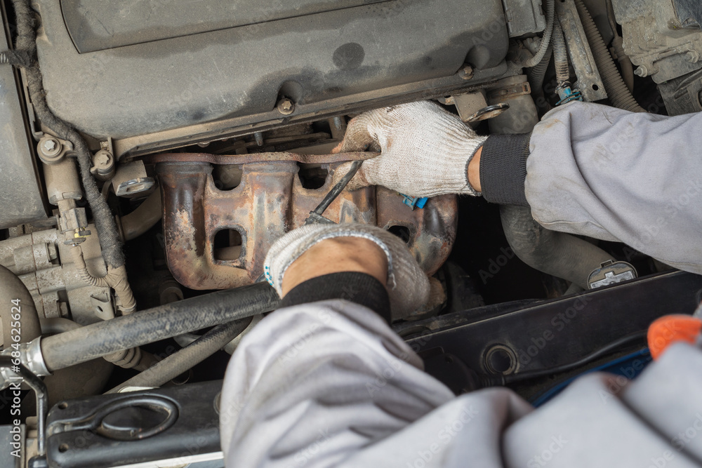 An auto mechanic removes the exhaust manifold to collect and remove ...