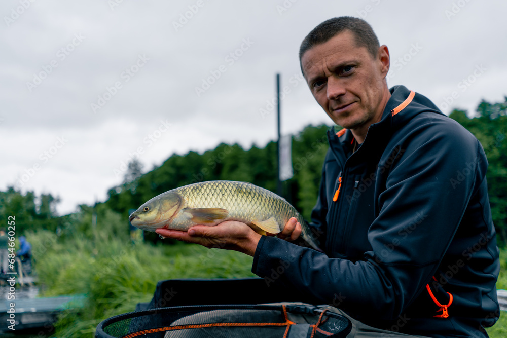 portrait of a professional fisherman holding a carp fish on the bank of ...