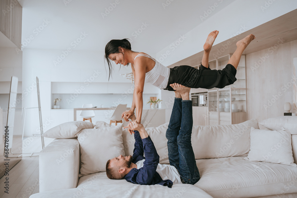 Young man lifts up girlfriend up laying on couch at home, having fun ...