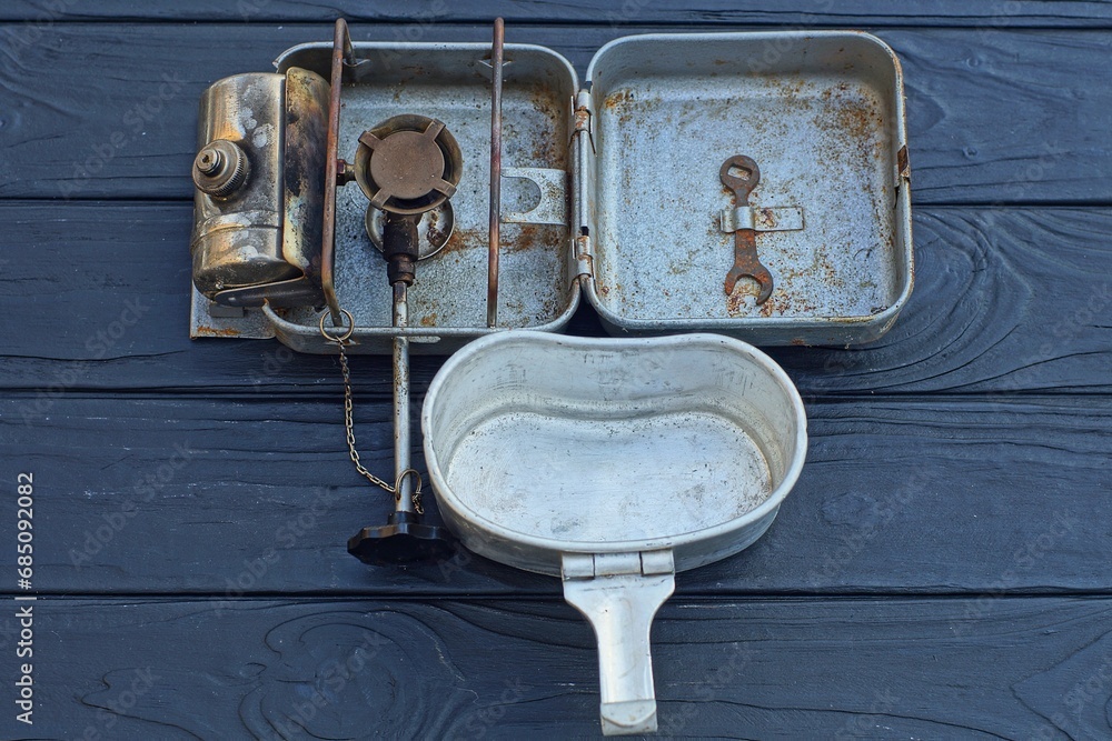 an aluminum empty old camping mug with a handle stands near an iron ...