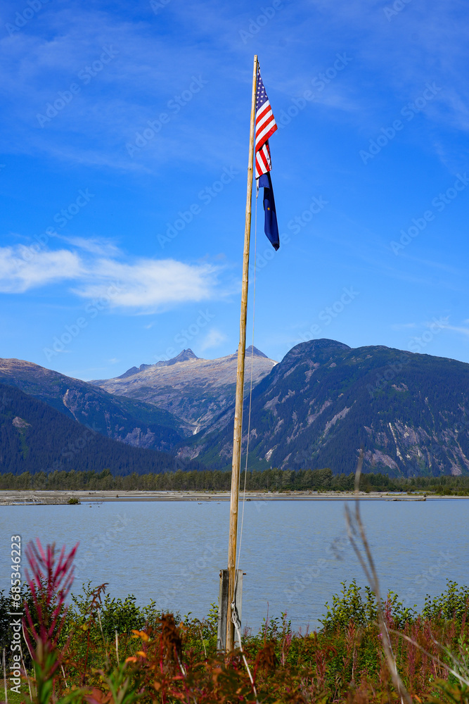 United States and Alaskan flags hanging at the top of a wooden flagpole ...