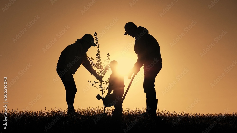Child watering tree seedling with parents silhouettes in disk country ...