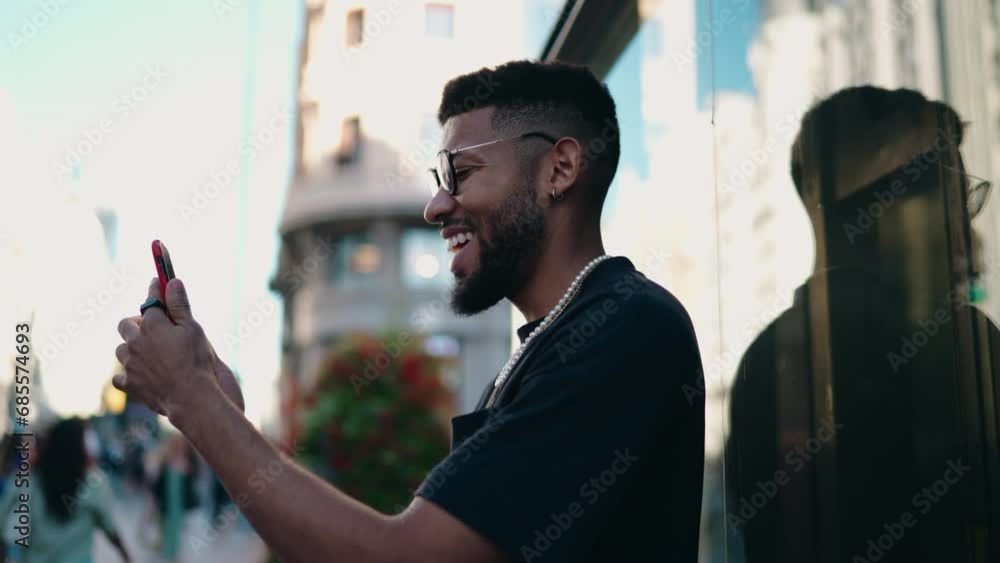 Smiling young man in casual wear using red smartphone on bustling city ...