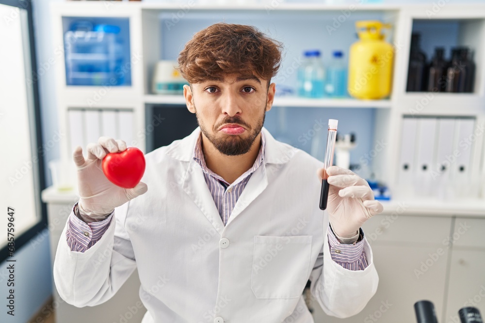 Arab man with beard working at scientist laboratory holding blood samples depressed and worry ...