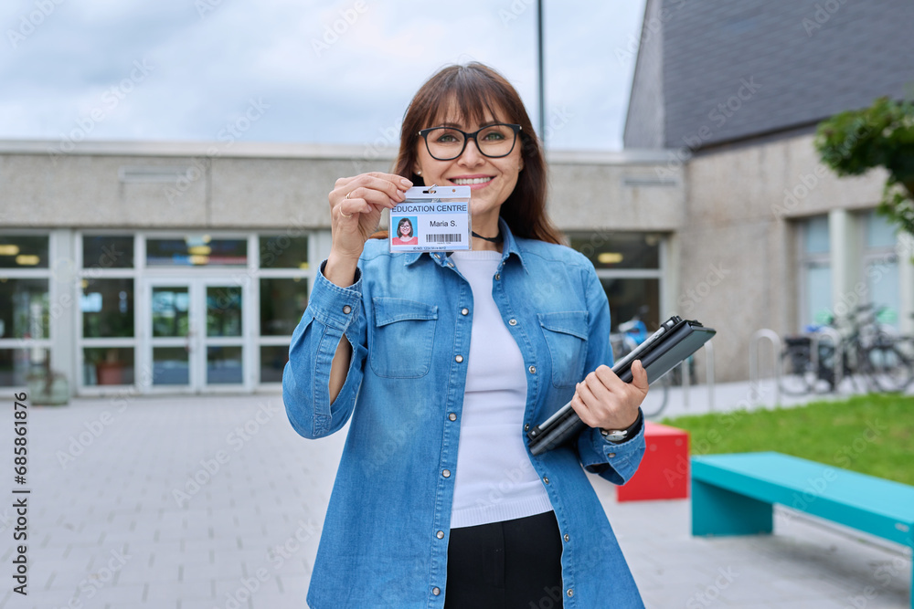Female teacher showing ID card badge, outdoor educational building ...