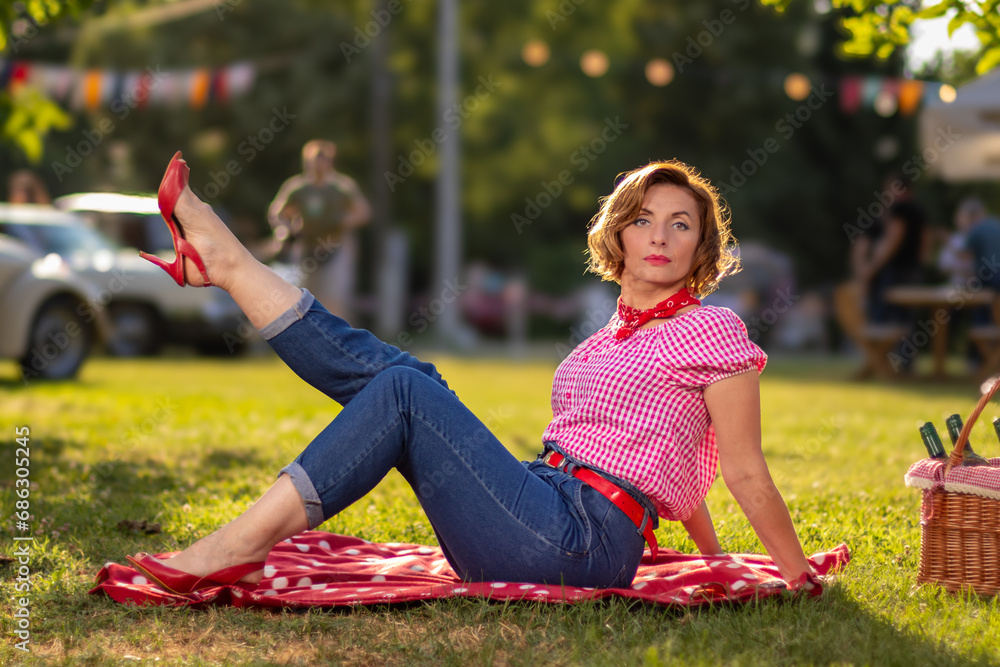 Pin-up woman lying on a picnic blanket on the grass with the sun ...