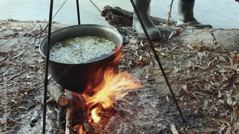 Video „a man adds branches to the fire, cooks fish soup in a cauldron ...