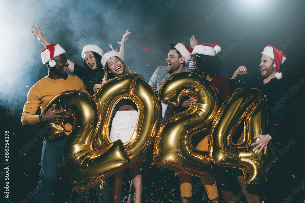 Happy young people holding 2024 shaped gold balloons while celebrating ...