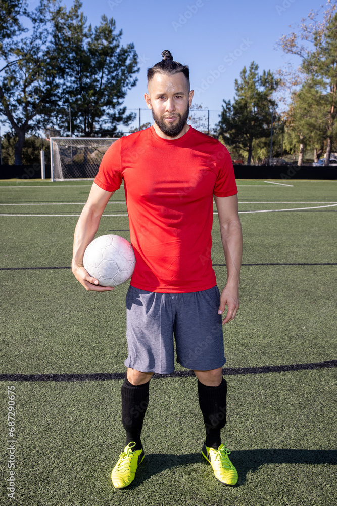 Strong man holding a soccer ball. The football player is wearing a red ...