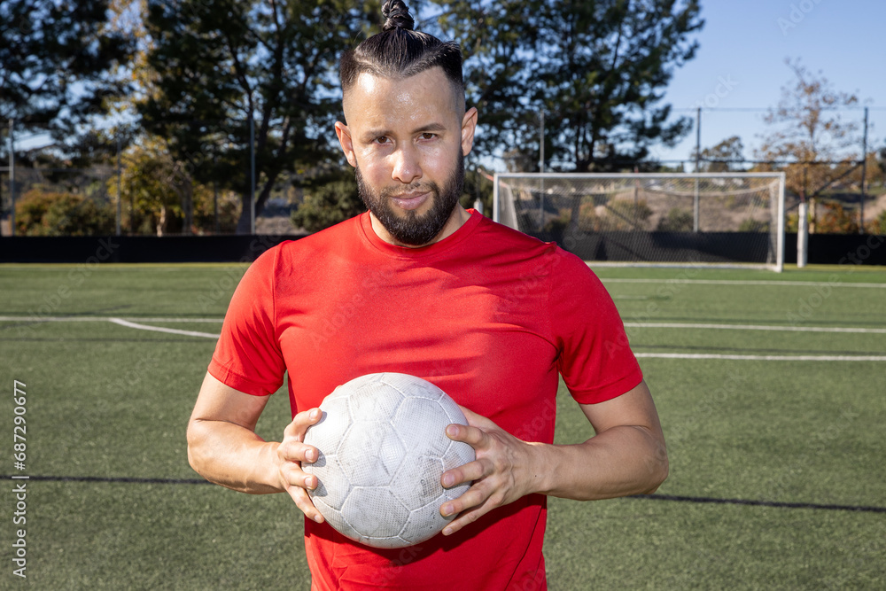 Strong man holding a soccer ball. The football player is wearing a red ...