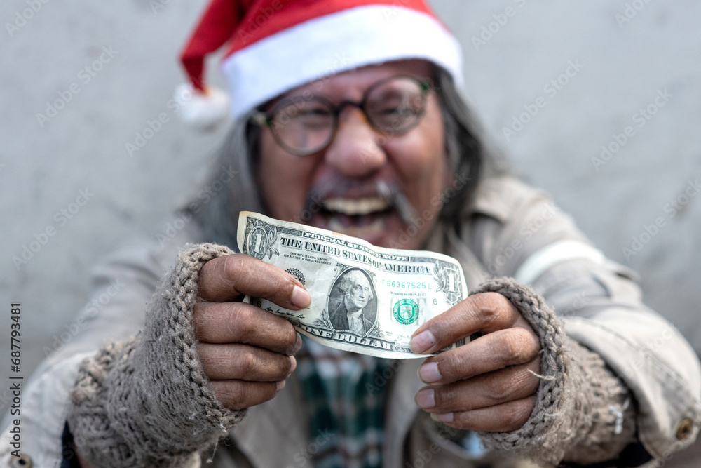 Homeless old man wearing a Santa hat laughs happily with a dollar bill ...