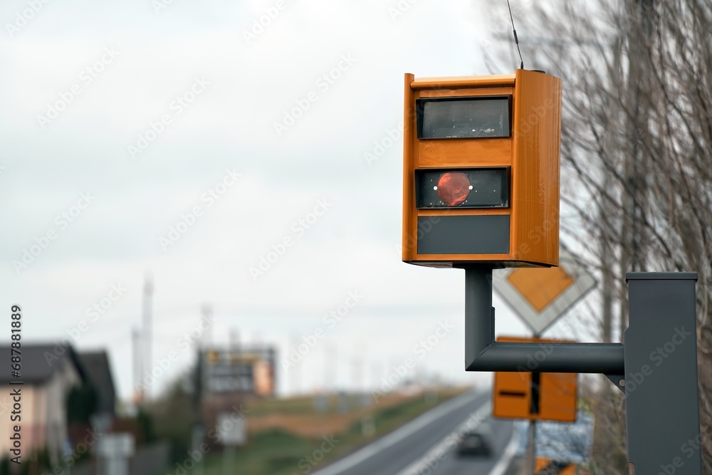 A yellow speed camera flashes as it detects a speeding car on a highway ...