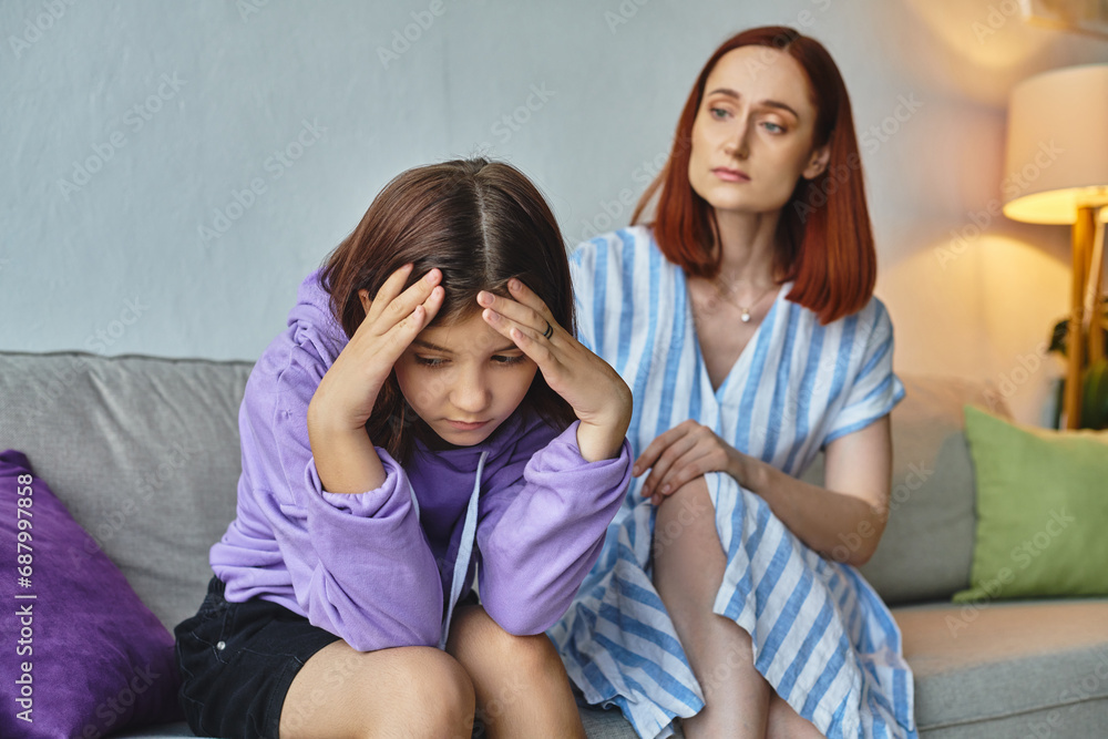 worried mother calming depressed teenage daughter sitting with bowed head on couch at home ...
