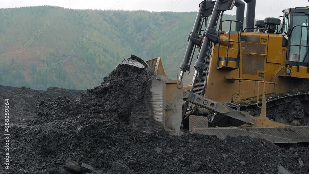 Heavy bulldozer pushing the black soil at the open-pit mine. Heavy ...