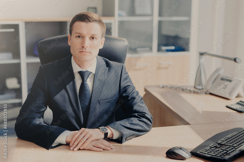 Serious businessman seated at a desk in a well-lit office, poised and ...