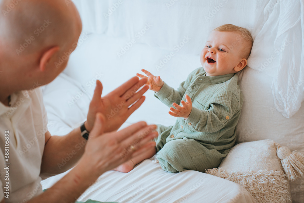 Foto de young dad claps his hands, plays with a baby boy on the bed ...