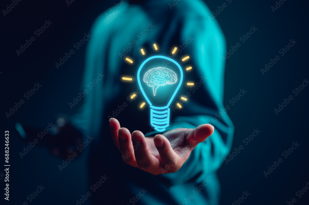 Hand holding drawing virtual lightbulb with brain on dark blue background for creative and smart ...