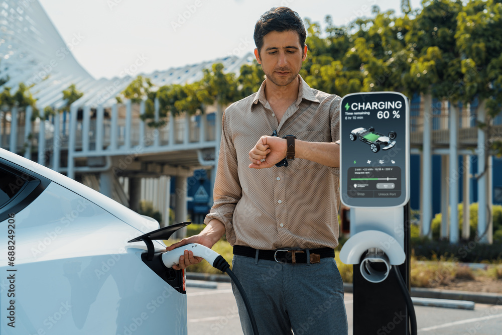 Young man checking time on smartwatch while EV charger to recharging ...