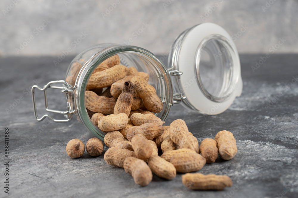 Glass jar full of fried peanuts in shell placed on a stone background ...