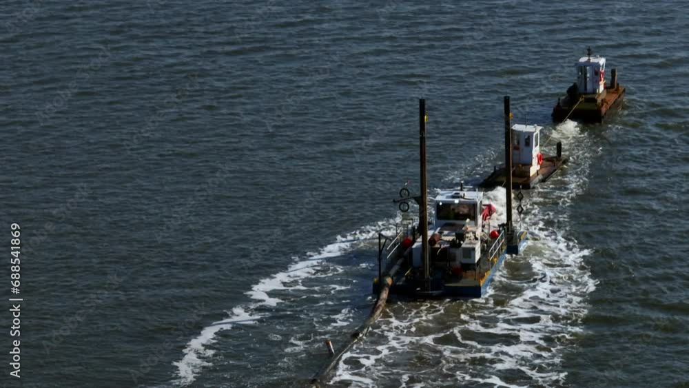 An aerial view of two tugboats, and a small barge dredging a bay on ...