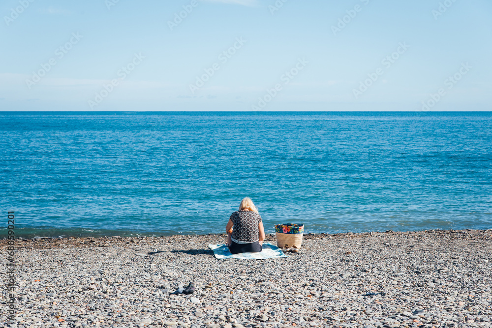 une femme assise seule sur la plage face à la mer. Une personne de dos ...