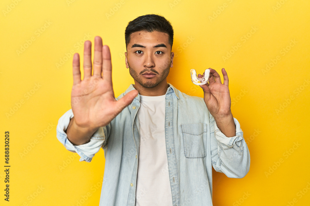 Asian man with invisible dental corrector, yellow studio backdrop ...